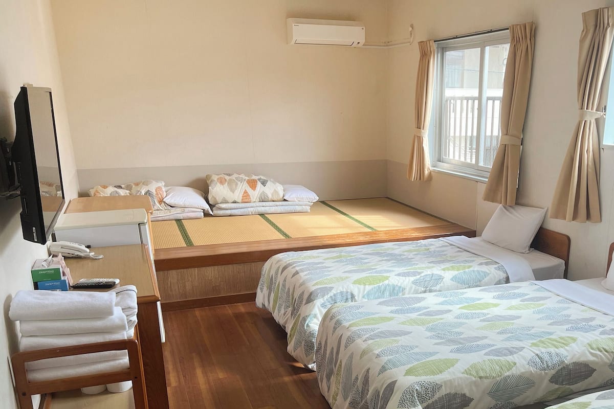 Quarto de hotel com duas camas, uma mesa com telefone e uma cadeira, televisão e janela com cortinas.