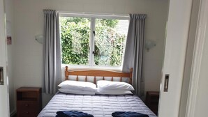 Cama bem arrumada com cabeceira, duas mesas de cabeceira e janela com cortinas.