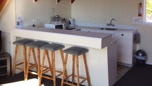 Cozinha compacta com bancada branca, quatro banquetas e janela com vista.