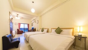 Quarto de hotel com duas camas, uma escrivaninha, uma cadeira e vista para o mar.