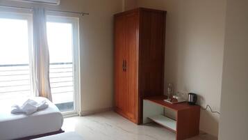 Quarto de hotel com cama, guarda-roupa de madeira, uma mesinha com chaleira e janela com cortinas.