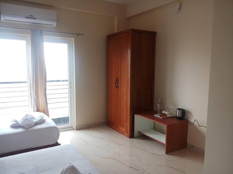 Quarto de hotel com cama, guarda-roupa de madeira, uma mesinha com chaleira e janela com cortinas.