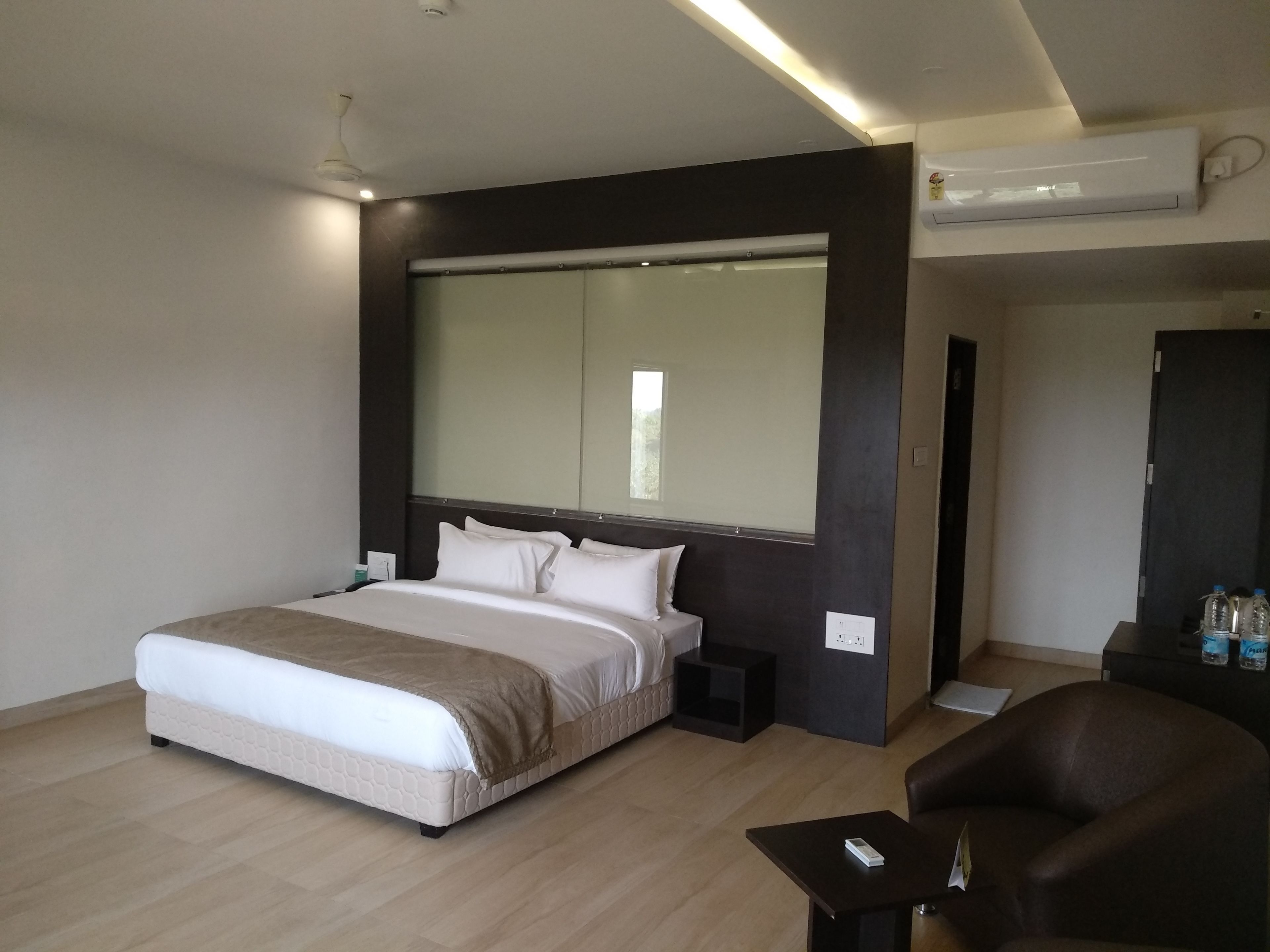 Quarto de hotel moderno com uma cama grande, mesa de cabeceira, uma cadeira e um espelho amplo.