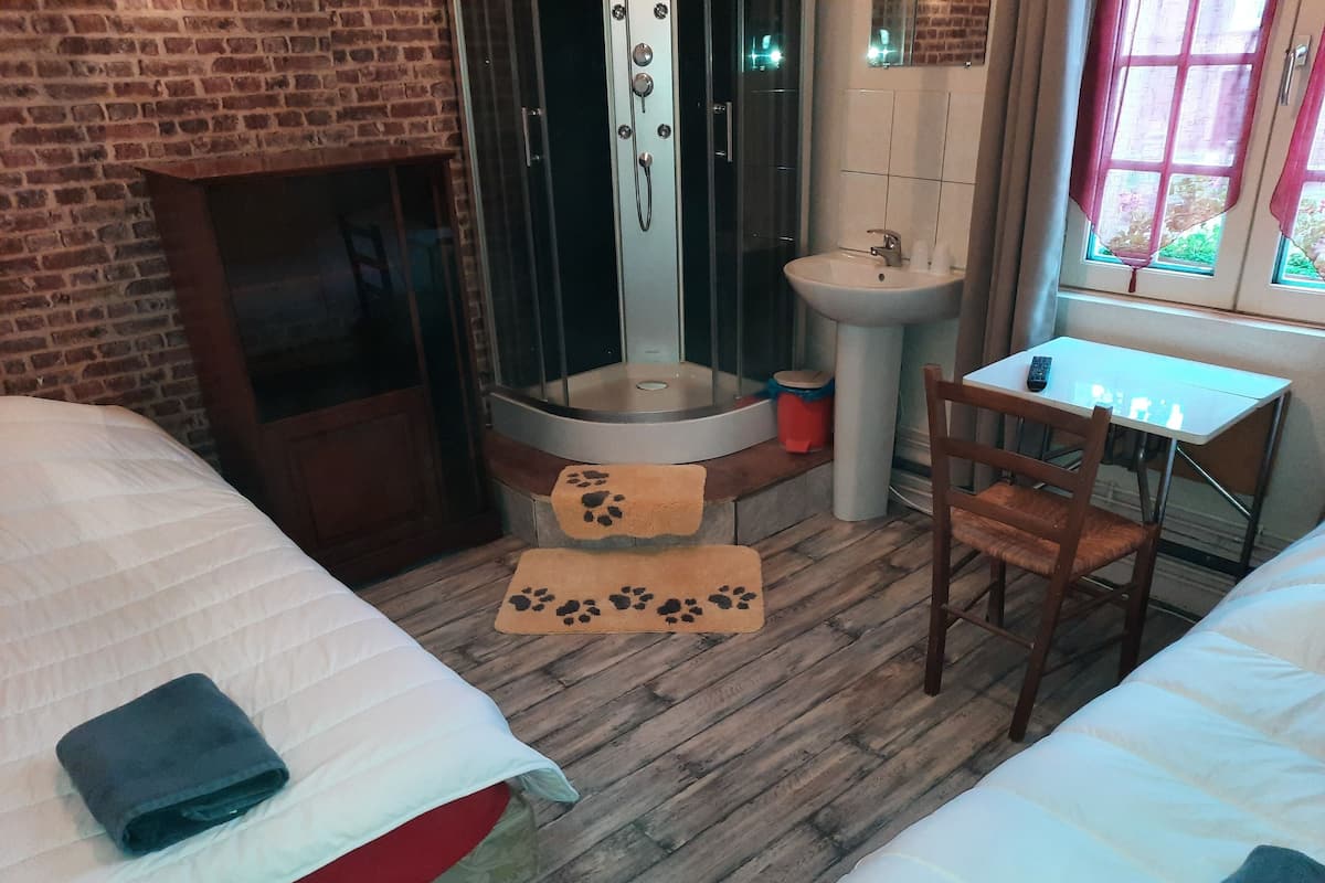 Quarto de hotel com duas camas, uma mesinha com um controle remoto, pia e janela com cortinas.