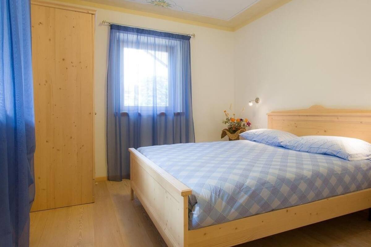 Quarto com cama de madeira, janela com cortinas azuis e guarda-roupa de madeira.