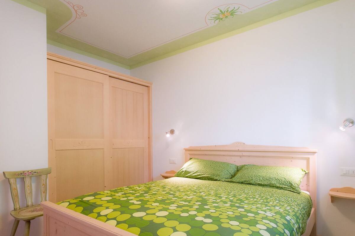 Quarto com cama, guarda-roupa de madeira e uma cadeira.