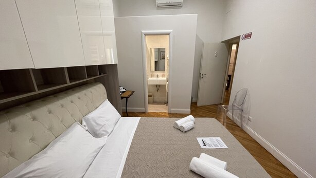 Quarto de hotel com uma cama, uma mesinha, um espelho e um banheiro visível por uma porta aberta.