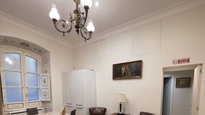Um quarto amplo com uma mesa de jantar, duas poltronas de couro, um candelabro, um quadro na parede e uma porta com uma placa.