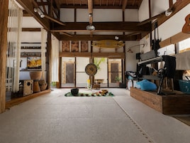 Um quarto espaçoso com teto alto, vigas de madeira, uma janela grande e diversos objetos, incluindo um brinquedo de pelúcia azul, um tambor e uma guitarra.