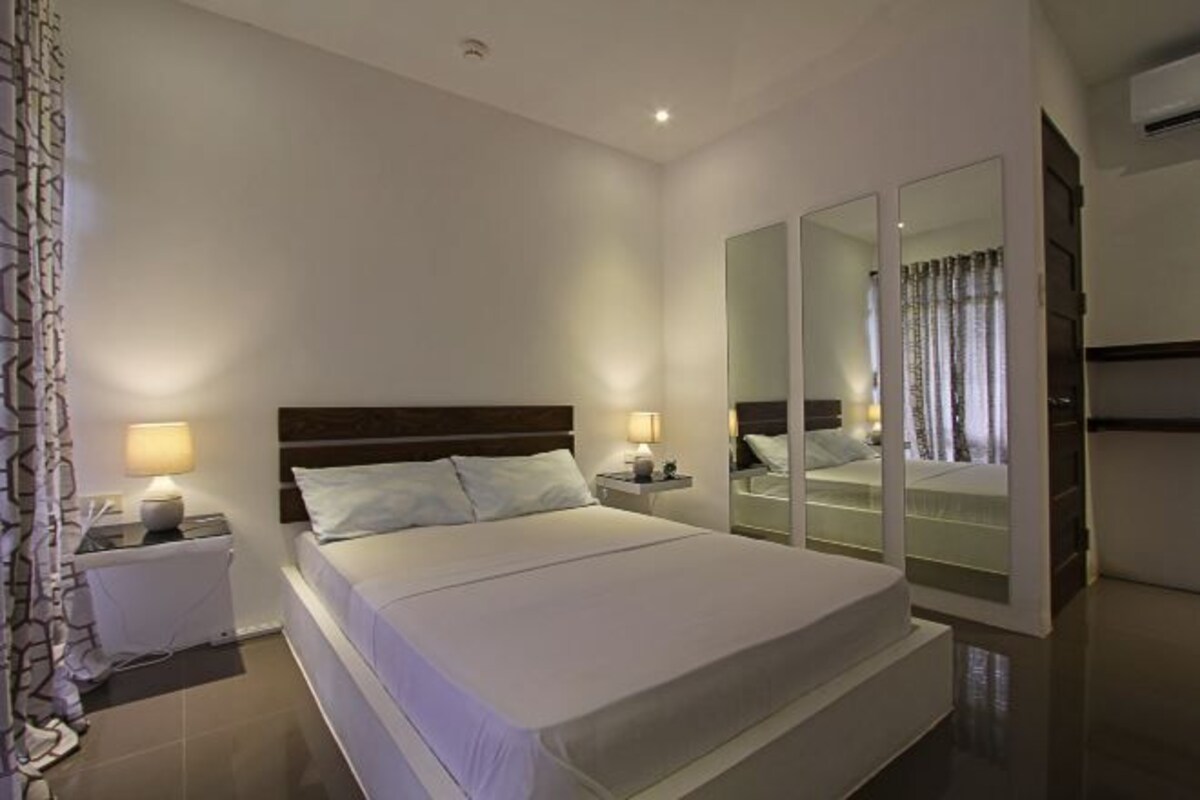 Quarto de hotel moderno com uma cama grande, abajures, um espelho e um guarda-roupa.