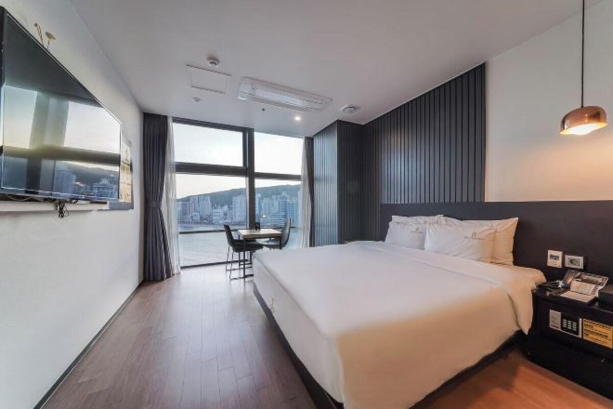 Quarto de hotel moderno com uma cama grande, uma escrivaninha e uma televisão.