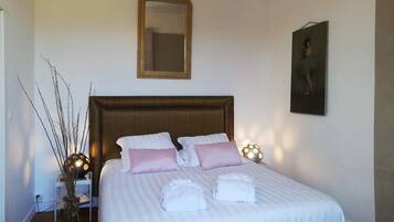 Cama bem arrumada com lençóis branco e rosa, cabeceira de madeira e duas luminárias de apoio.
