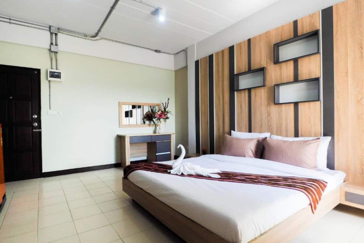 Quarto de hotel com uma cama grande, parede de destaque em madeira, escrivaninha com espelho e um vaso com flores.