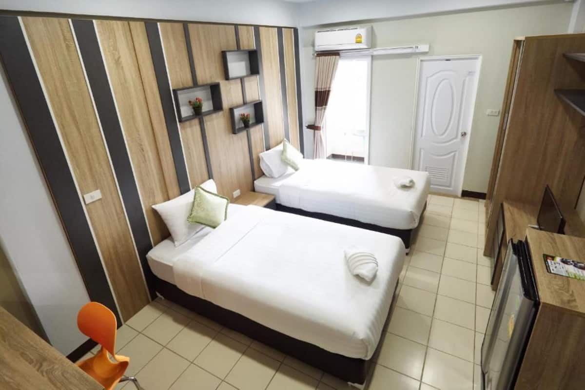 Quarto de hotel com duas camas, uma escrivaninha, uma cadeira, um guarda-roupa e um ar condicionado.