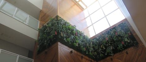 Teto alto com claraboia, painéis de madeira e parede verde com plantas.