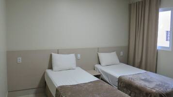Quarto de hotel com duas camas de solteiro, uma janela com cortinas e uma parede lisa.