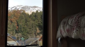 Quarto com janela vista para uma montanha nevada e árvores de outono.