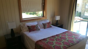 Quarto com cama, duas mesas de cabeceira, janela com persiana e vista para o exterior.