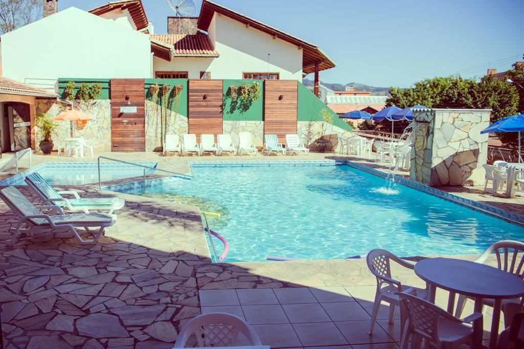 Uma piscina com espreguiçadeiras e guarda-sóis, cercada por azulejos de pedra e um edifício com telhado telhado.