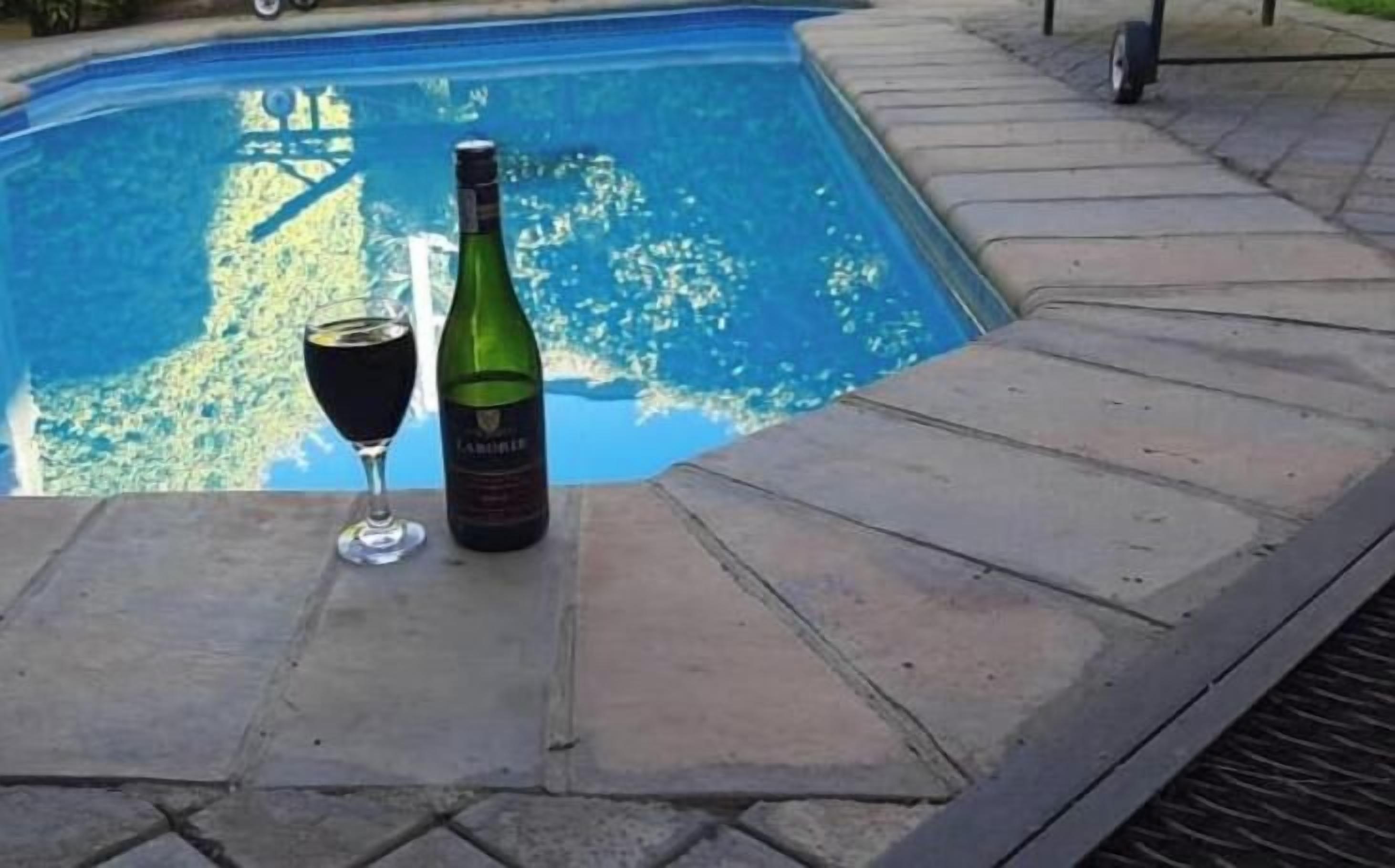 Cenário à beira da piscina com uma garrafa e um copo de vinho.
