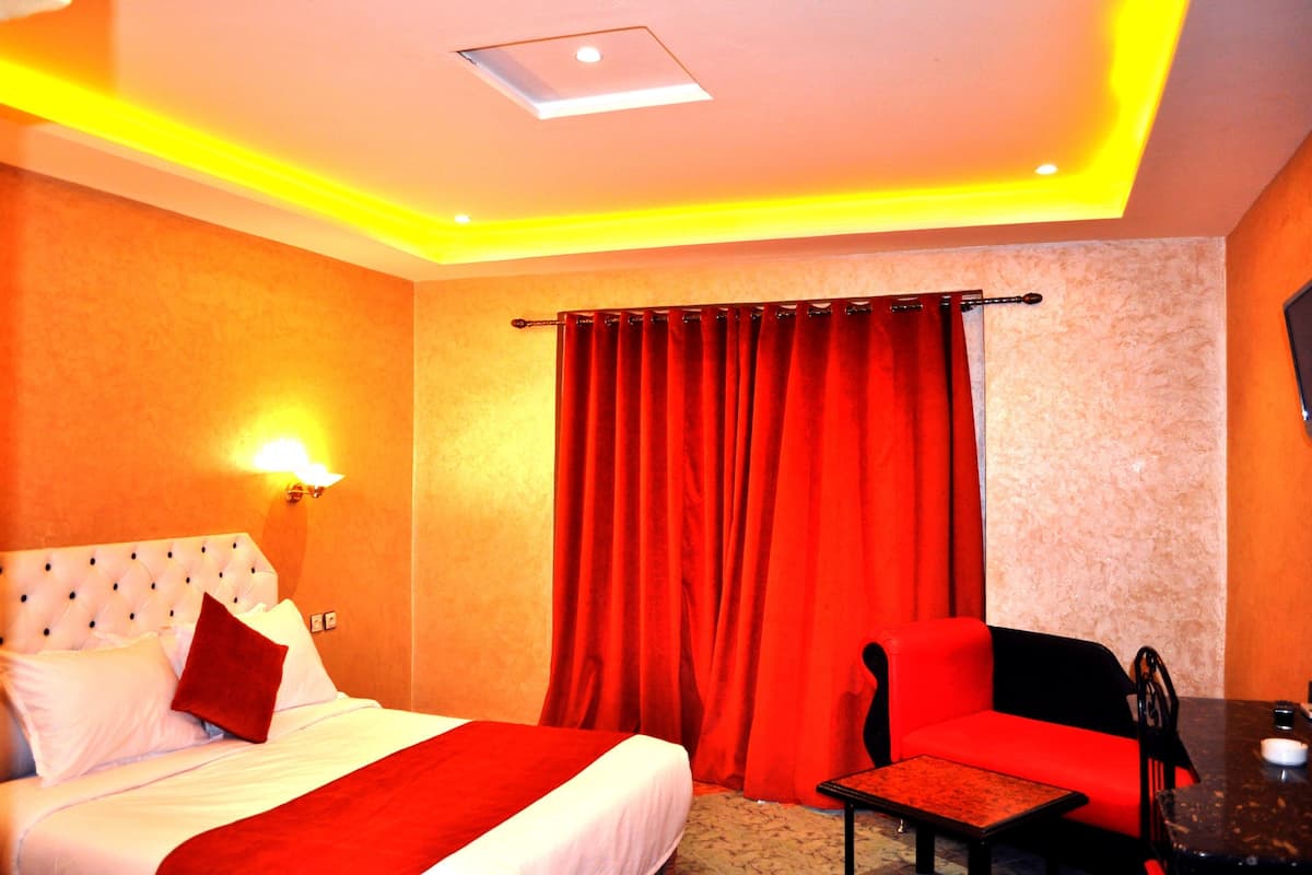 Quarto de hotel com cama, cortinas vermelhas, uma mesinha e uma cadeira.