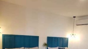 Duas camas de solteiro com cabeceiras azuis, roupa de cama branca e piso de madeira.