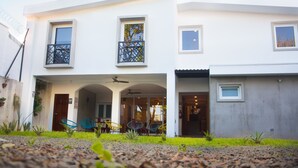 Uma casa de dois andares com varanda, alpendre coberto e um jardim com cadeiras.