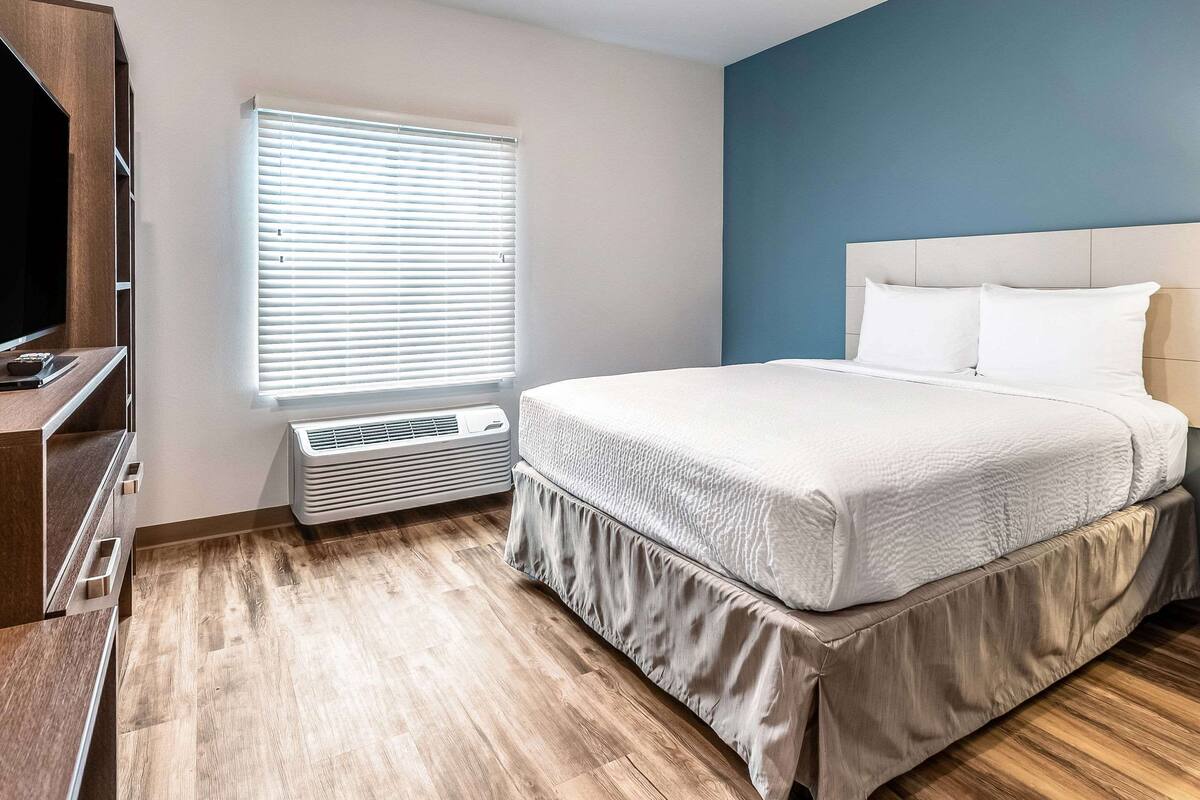 Quarto de hotel com cama, televisão, janela com persianas e aquecedor de parede.