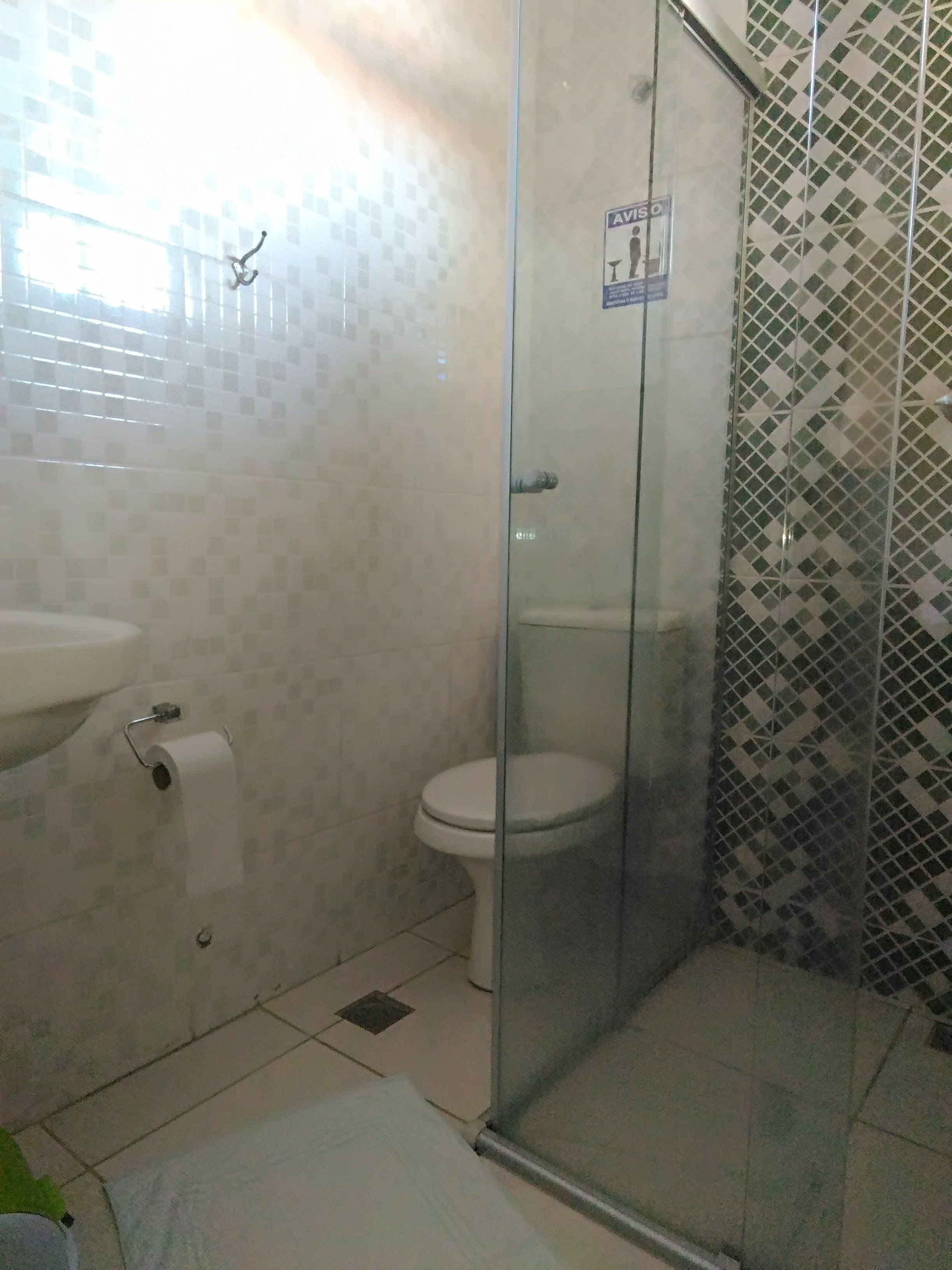 Uma casa de banho com chuveiro em cabine de vidro, sanita e lavatório com suporte para papel de cozinha.
