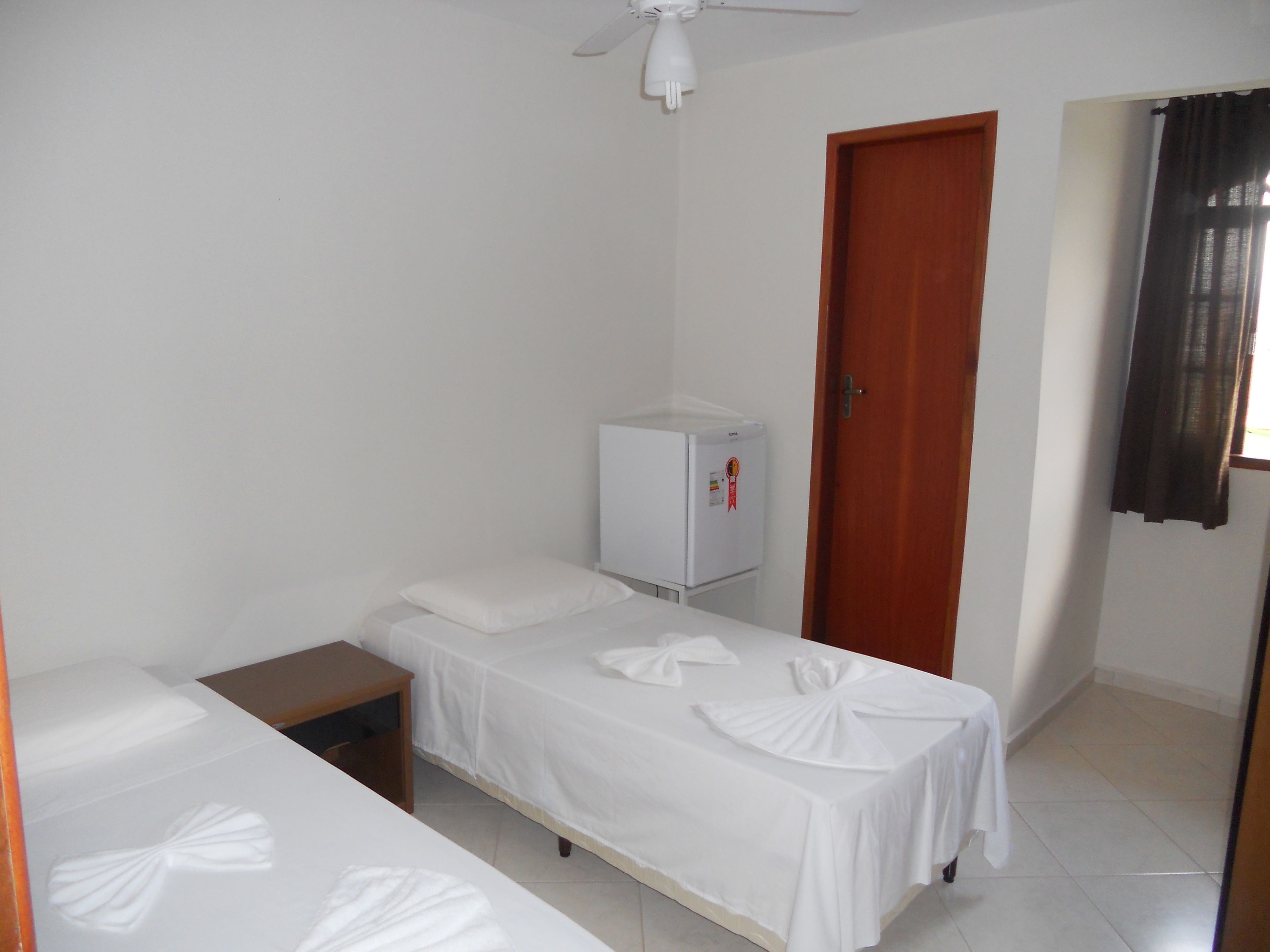 Quarto pequeno e limpo com uma cama de solteiro, mesa de cabeceira, armário pequeno e uma porta.