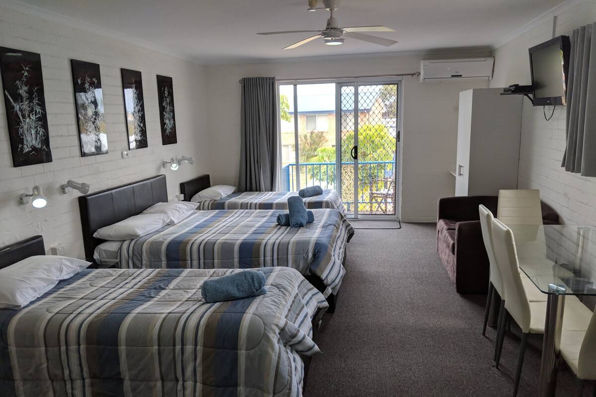 Quarto de hotel com duas camas, uma escrivaninha, uma cadeira, televisão e varanda com vista.