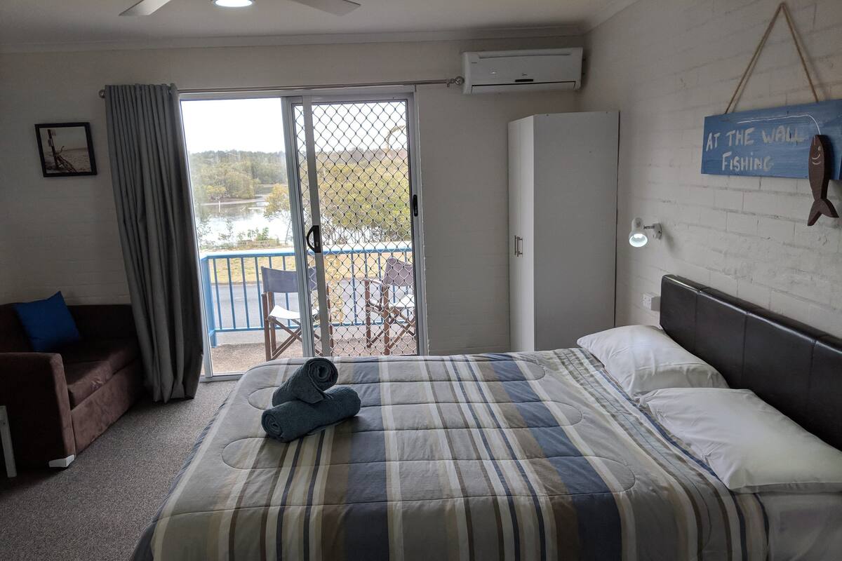 Um quarto com cama, janela com cortinas, uma cadeira e um aviso na parede.
