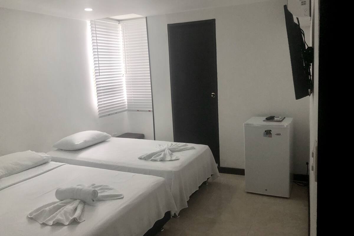 Quarto de hotel com duas camas, um frigorífico pequeno e uma porta.