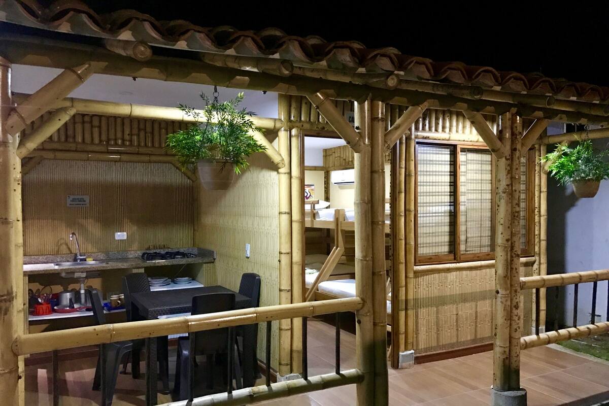 Quarto com decoração em bambu, área de refeições, pequena cozinha e uma janela.