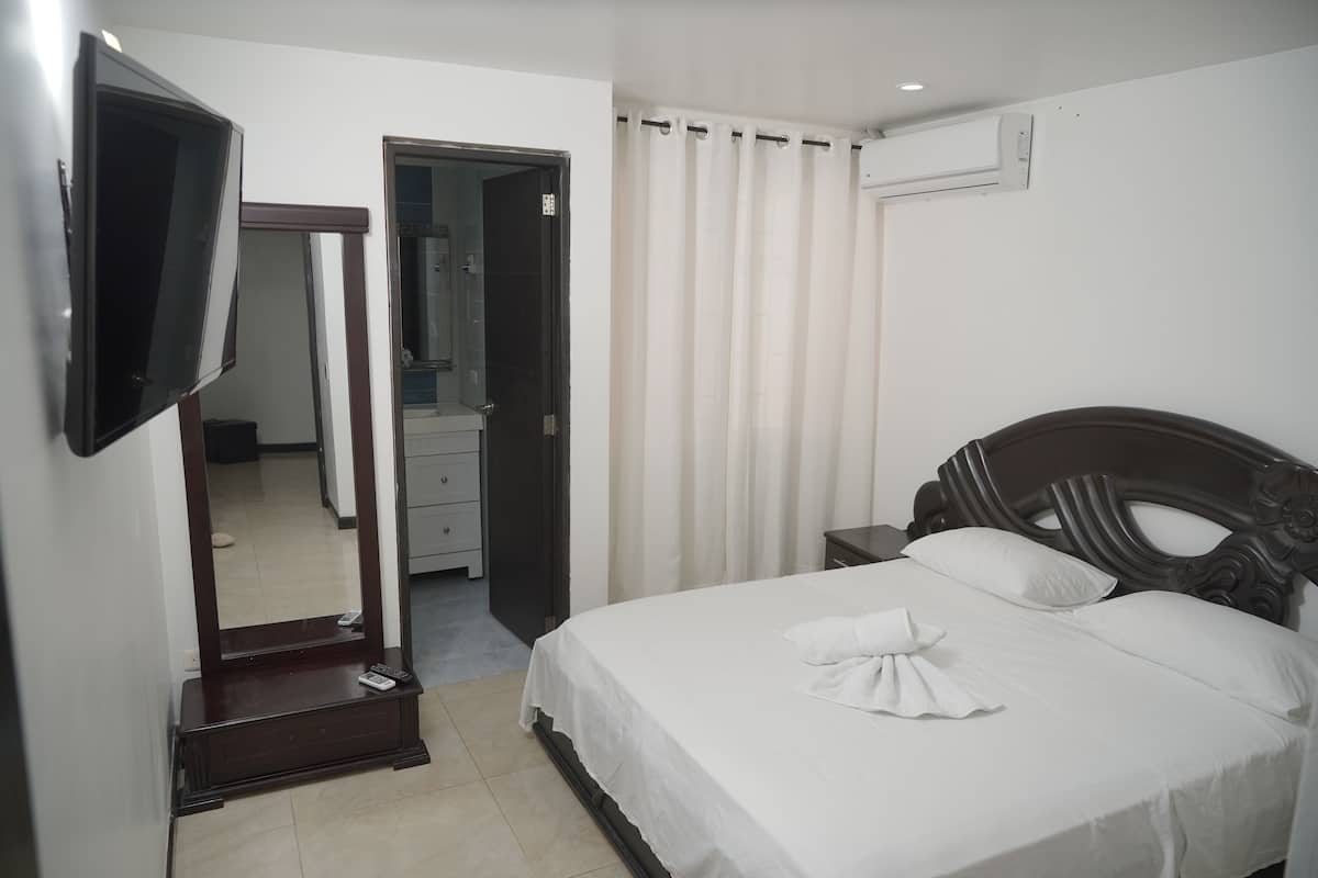 Quarto de hotel com cama, espelho, televisão, guarda-roupa e cortina.
