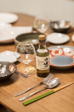 Uma garrafa de The Yamazaki Single Malt Whisky sobre uma mesa de madeira, com pratos, um copo, hashis e talheres.