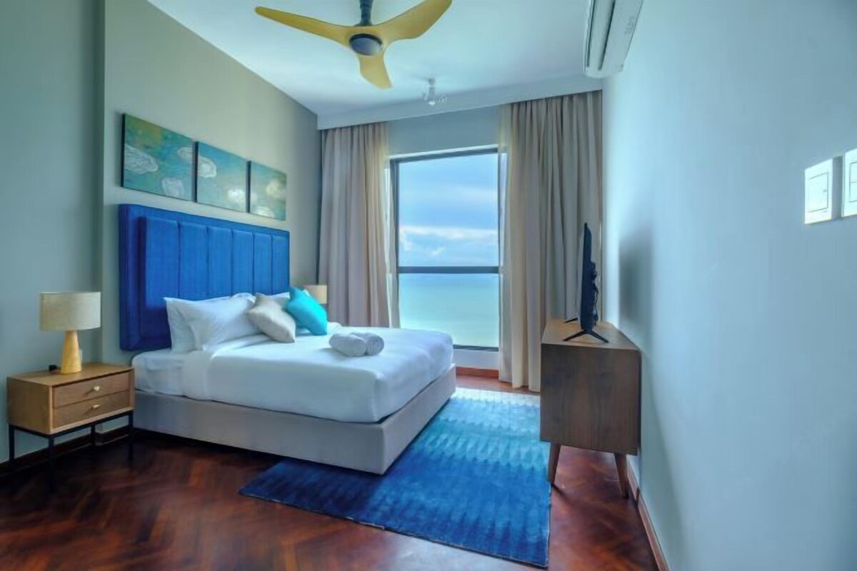 Quarto de hotel com uma cama grande, um ventilador de teto, televisão e vista para o oceano.