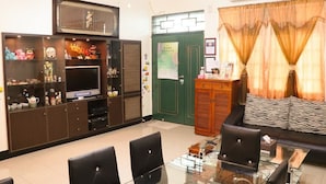 Uma sala de estar com um sofá, cadeiras, uma TV, um armário com objetos decorativos e uma porta com um pôster.