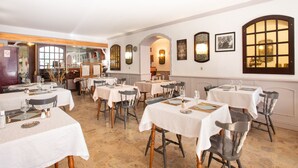 Um restaurante com várias mesas preparadas para refeições, com toalhas de mesa brancas e cadeiras de madeira.