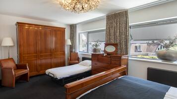 Quarto com cama, guarda-roupa, cadeira, penteadeira, espelho e janela com vista para o exterior.