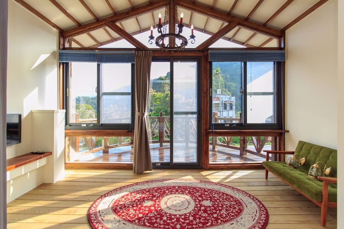 Um quarto amplo com grandes janelas, teto de madeira e sofá verde.