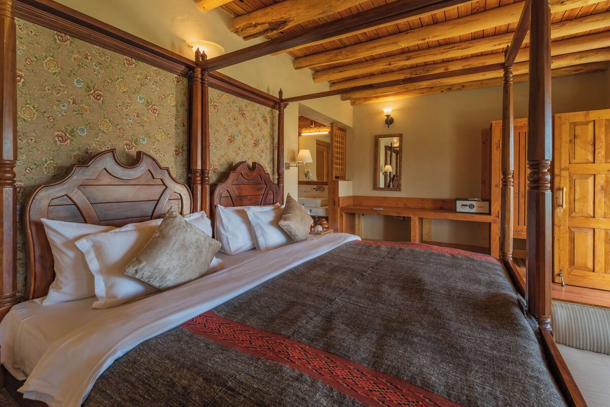 Uma cama de dossel com cabeceira de madeira, edredom estampado em vermelho e preto, e várias almofadas.