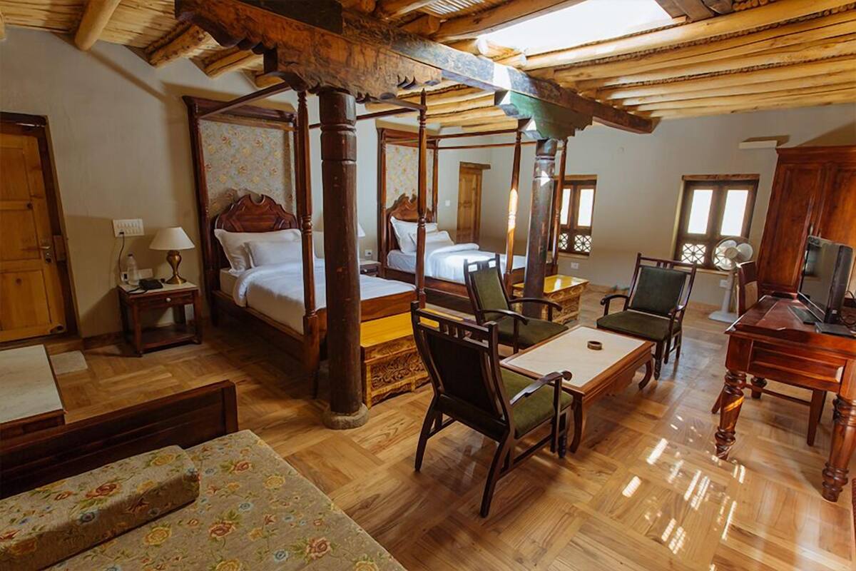 Uma cama tradicional com dossel e cabeceira floral, uma mesa de centro de madeira e um espaço de estar com cadeiras.
