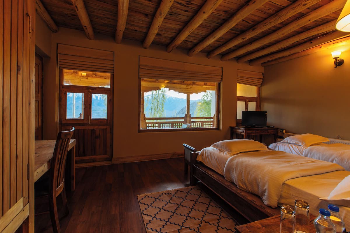 Quarto com piso de madeira, duas camas, uma escrivaninha e janela com vista para montanhas.