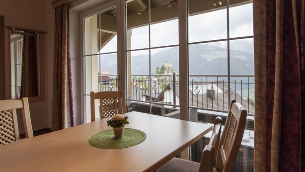 Uma área de refeições com mesa, cadeiras e vista para montanhas através de grandes janelas.