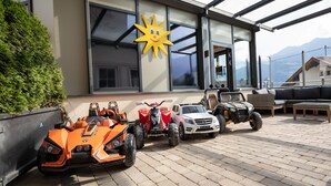 Um edifício com decoração em formato de sol, um carro branco e duas motocicletas todo-terreno estacionadas na frente.