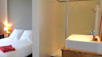 Quarto de hotel com cama, luminária de cabeceira, banheiro com chuveiro e pia.
