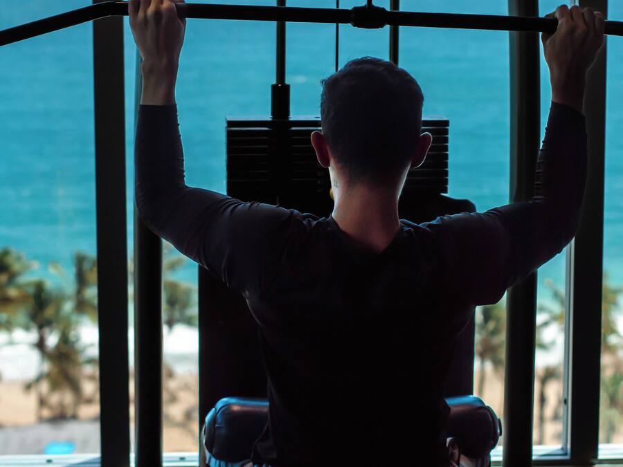 Uma pessoa se exercitando em uma barra de pull-up, com vista para o oceano através de grandes janelas.