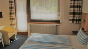 Quarto de hotel com uma cama, uma cadeira, uma janela com cortinas e um radiador.