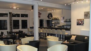 Uma área de bar moderna com banquetas altas, um balcão com garrafas e um espaço de estar com sofás e cadeiras.